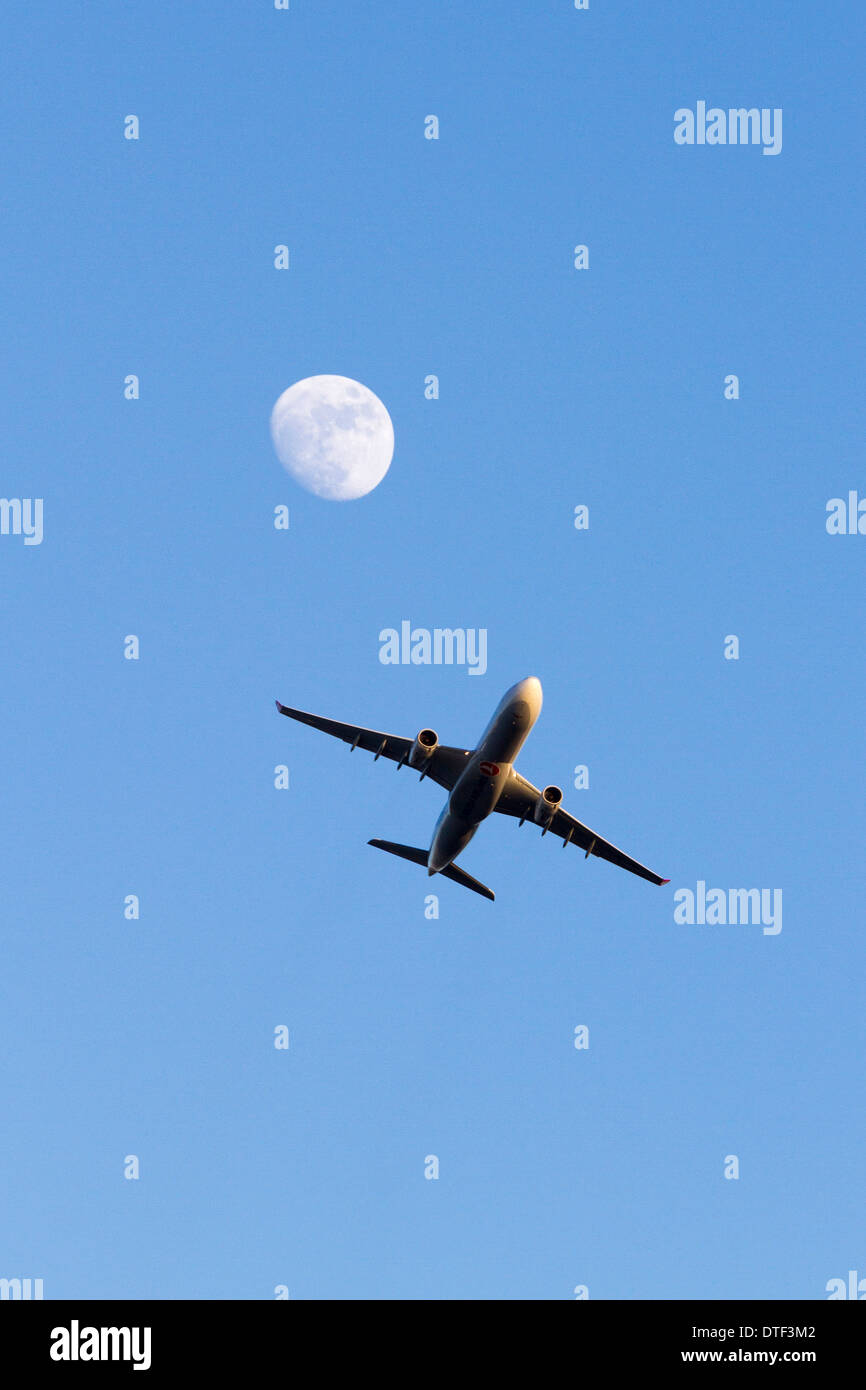 Plane flying across the sky with the moon in the background, England ...