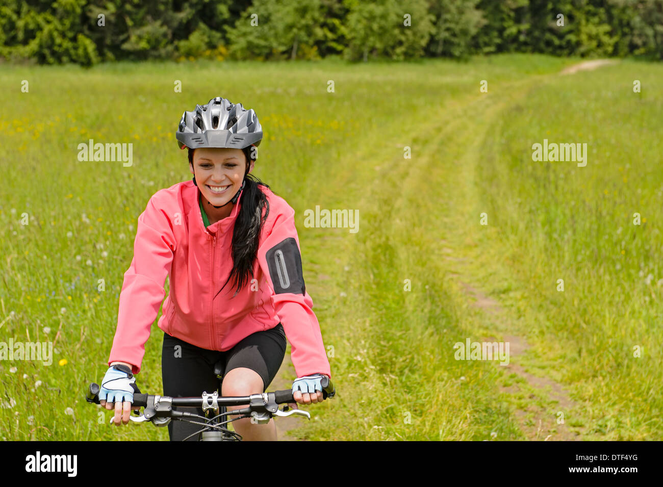 Woman riding bicycle on countryside path through meadow smiling Stock ...