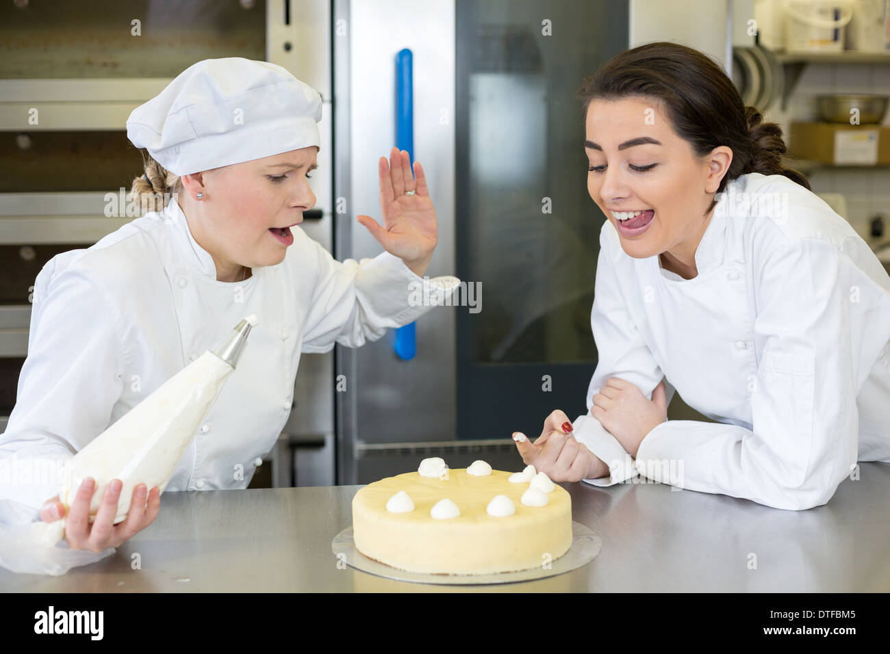 Confectioner apprentice nibbling whipped cream from cake in bakery ...