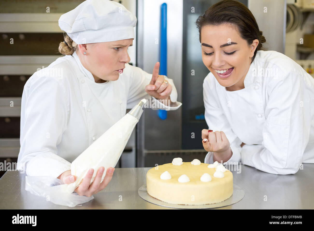 Confectioner apprentice nibbling whipped cream from cake in bakery ...