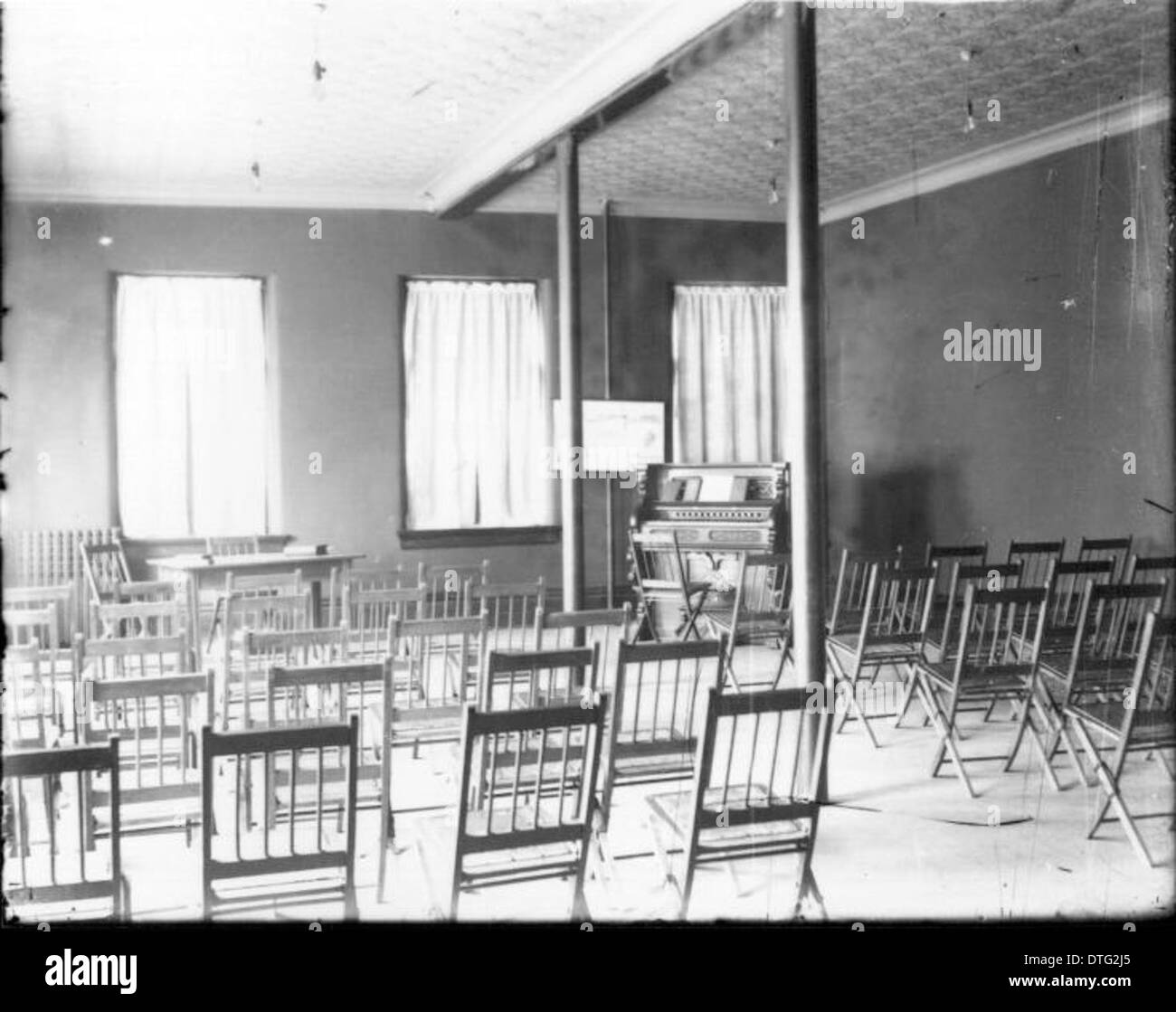 This photograph shows a room containing chairs and a pump organ ...