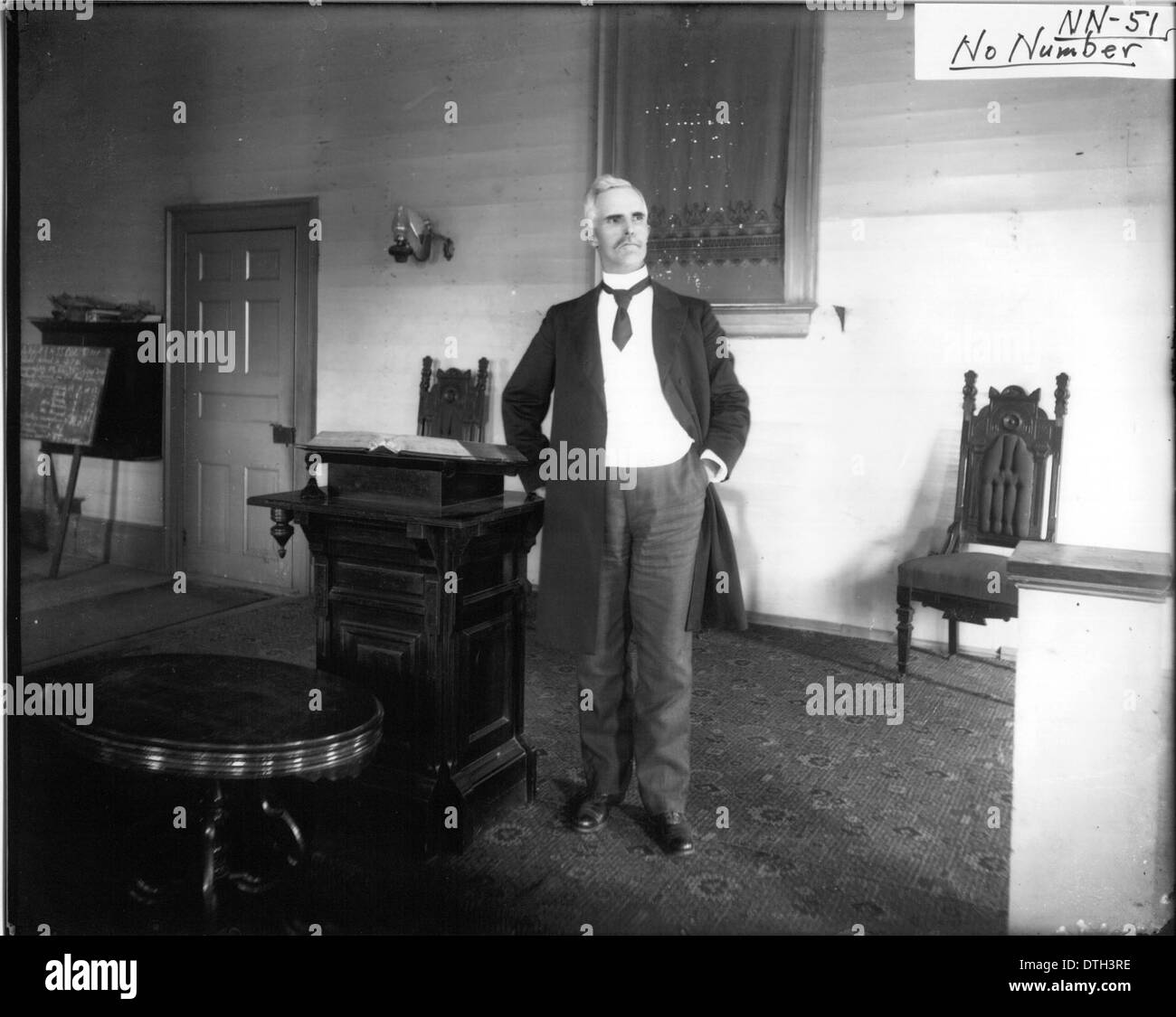 A historical photograph of a man standing near a podium, likely from ...