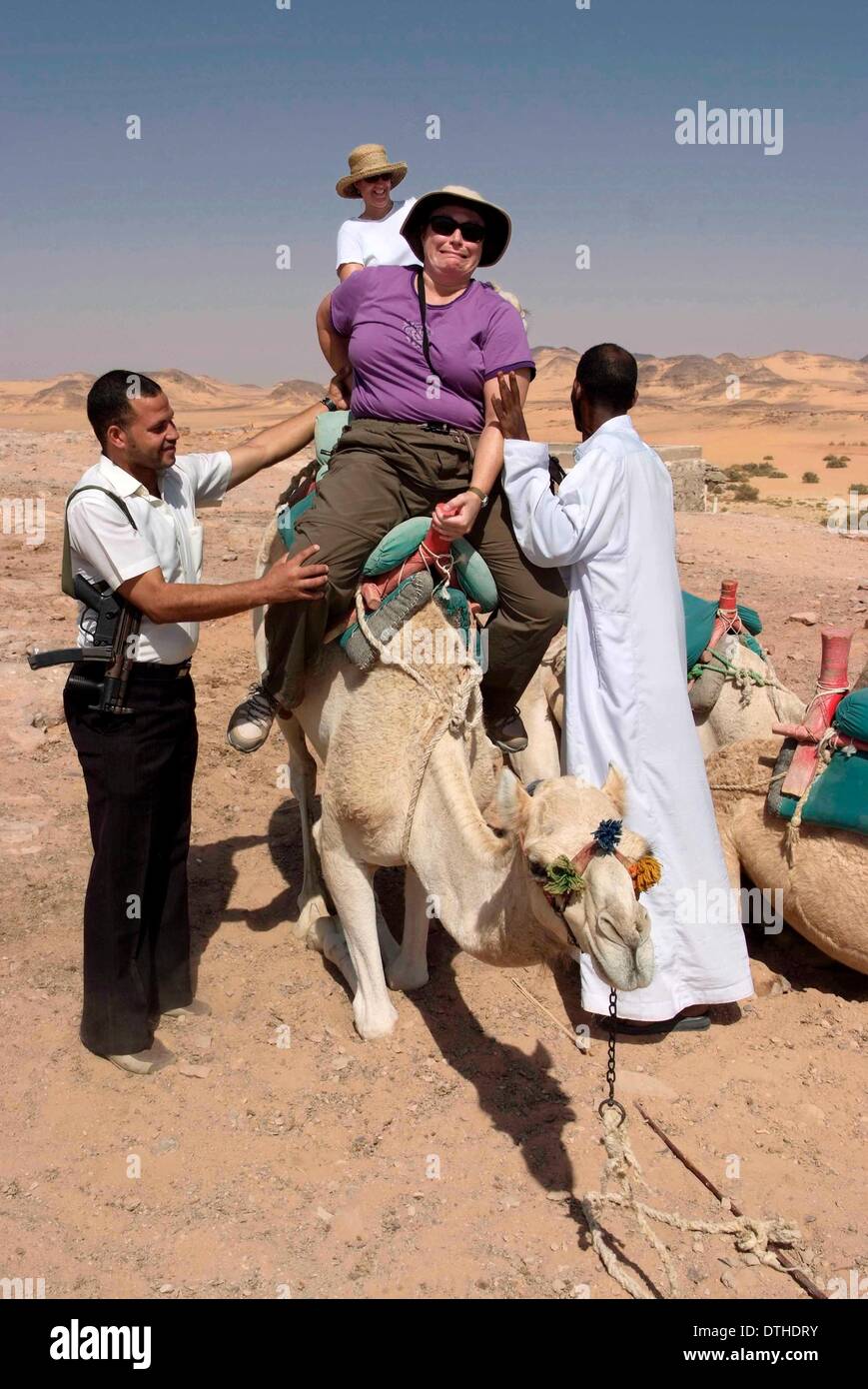EGYPT Armed plain clothes policeman helps a tourist dismount a camel ...