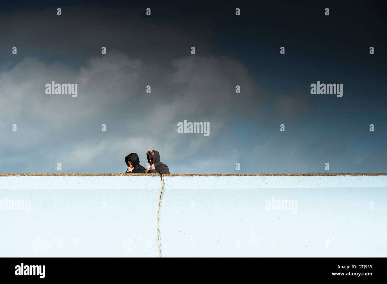Two people sheltering from the weather as they walk along the sea wall ...