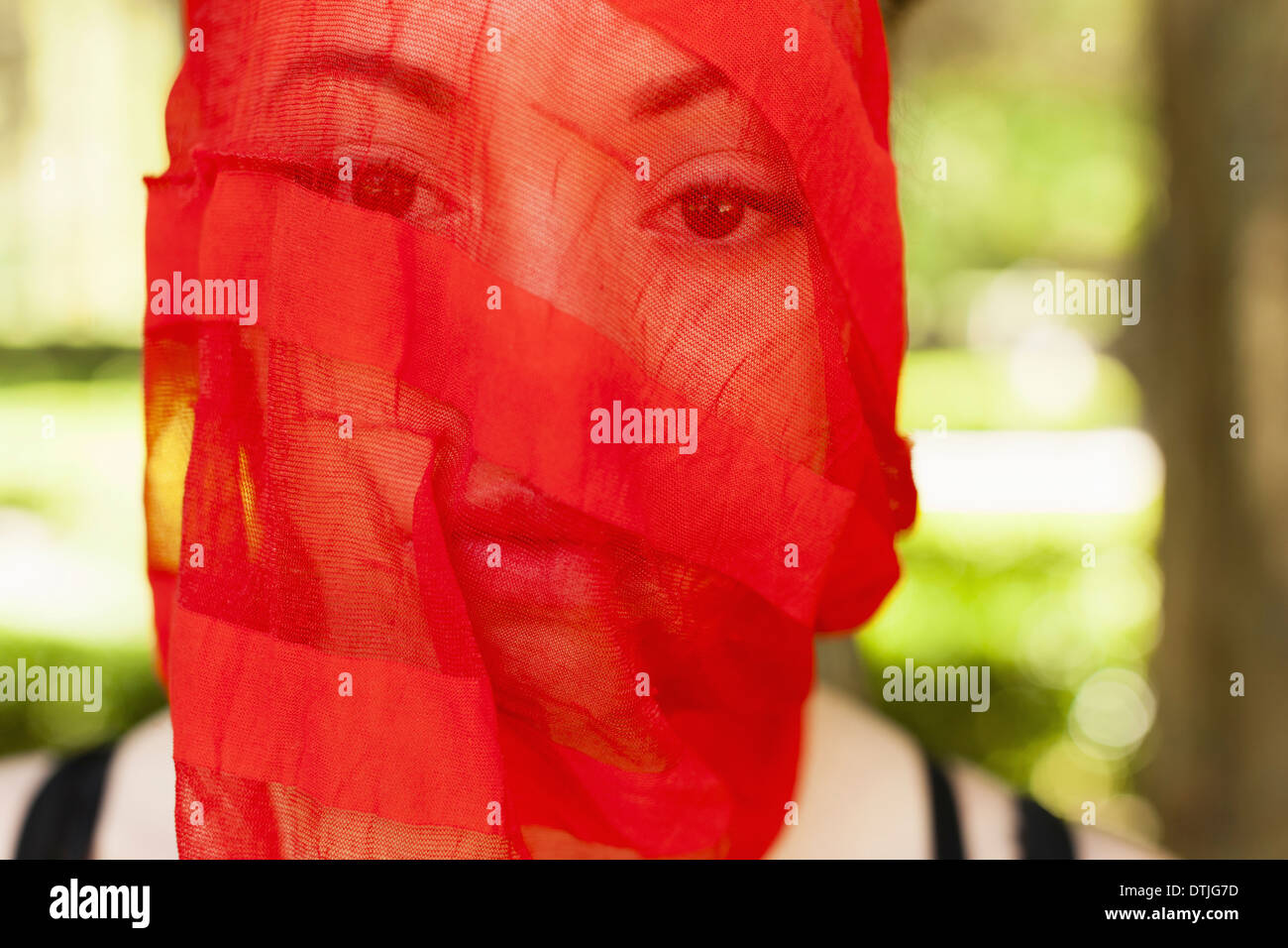 A young woman with a red seethrough sheer veil across her face ...