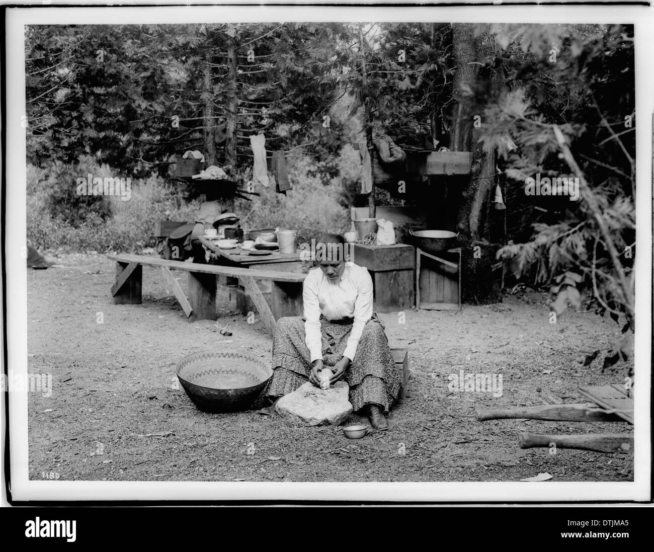A Paiute Indian woman grinding acorns using a traditional matate stone ...