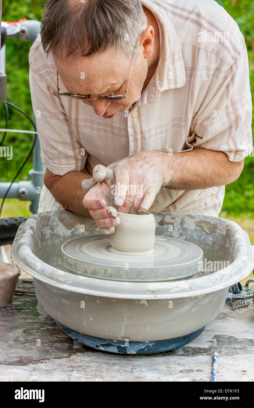 Man modeling wet clay pot on potters wheel outdoors at the Etruria ...