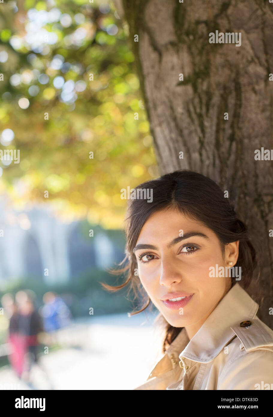 Woman standing against tree trunk in urban park Stock Photo - Alamy