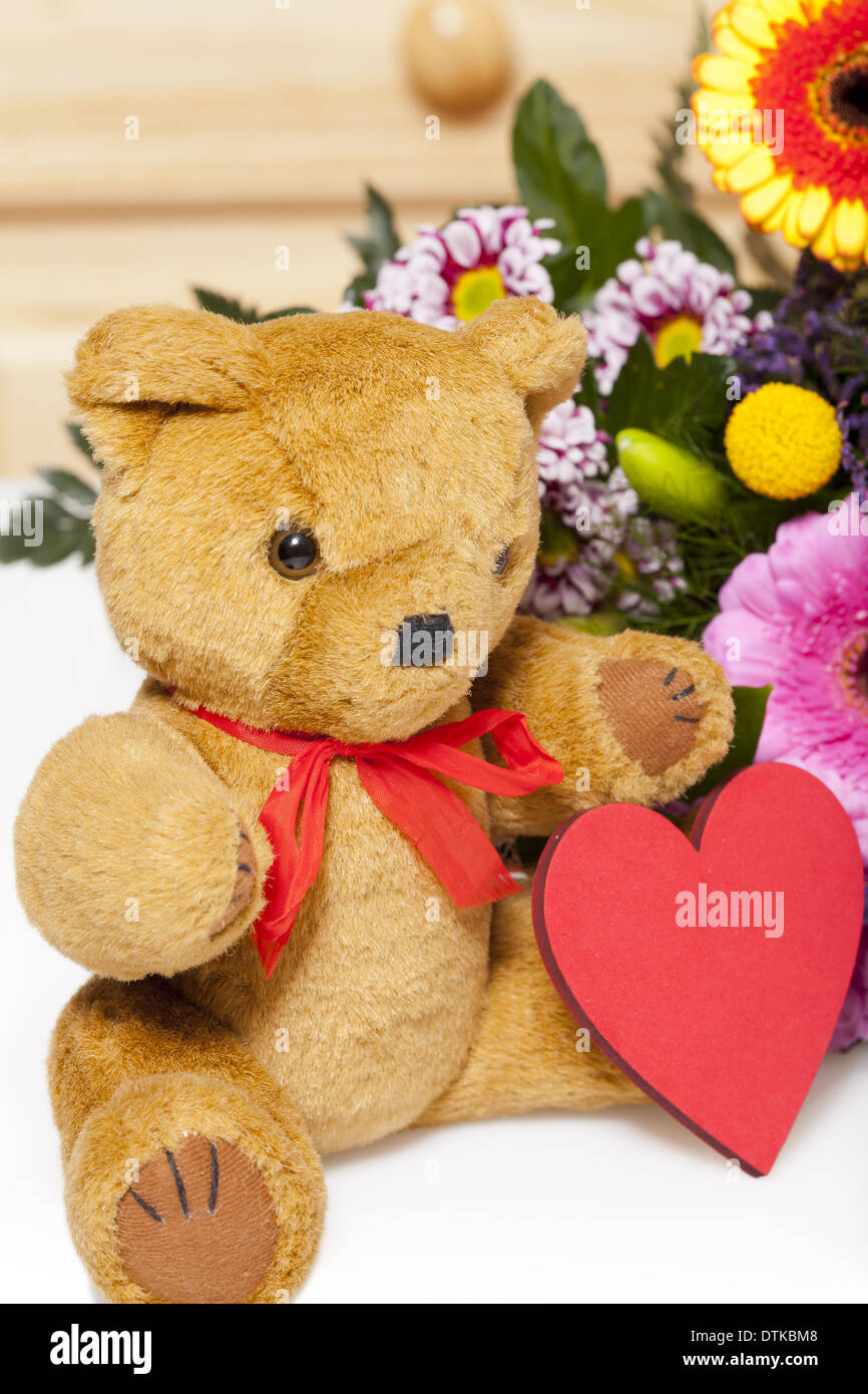 Plush Teddy with red heart, in the background a bouquet with copy space ...
