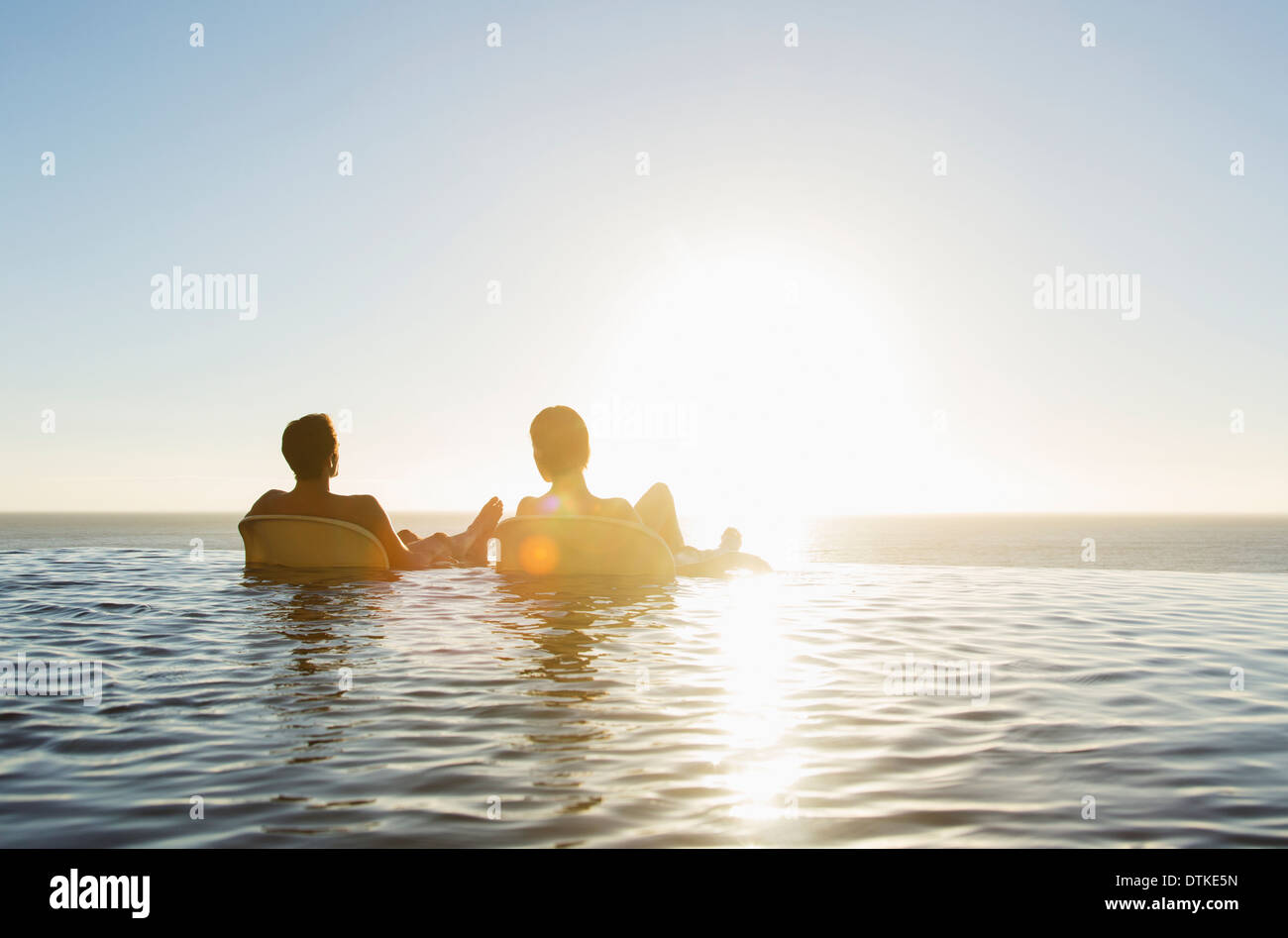 Couple in lounge chairs in infinity pool overlooking ocean Stock Photo ...