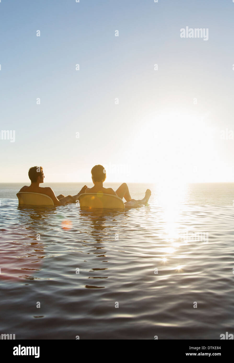 Couple in lawn chairs in infinity pool overlooking ocean Stock Photo ...