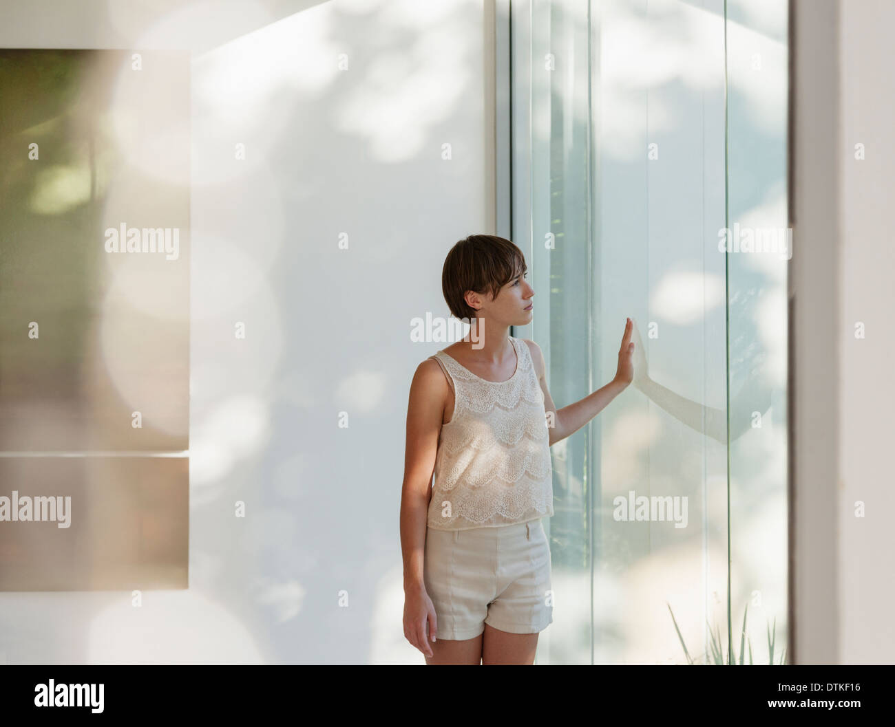 Pensive woman standing at sunny window Stock Photo - Alamy