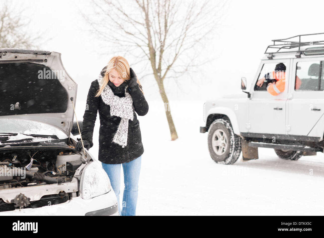 Woman looking under broken car hood snow Stock Photo - Alamy