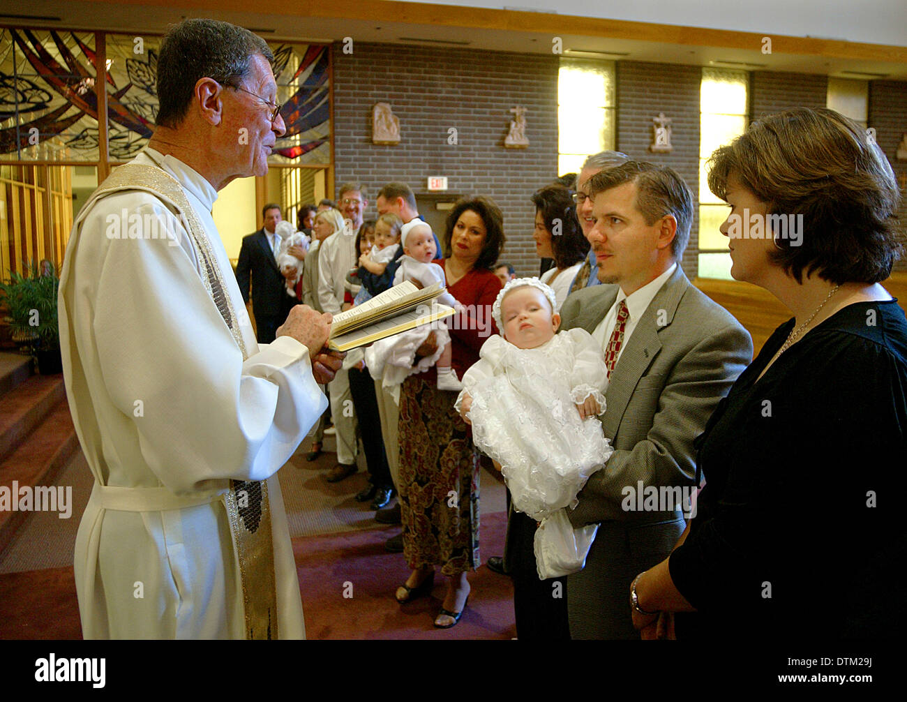 A robed Catholic priest reads a sermon to parents and children during christening ceremonies at ...
