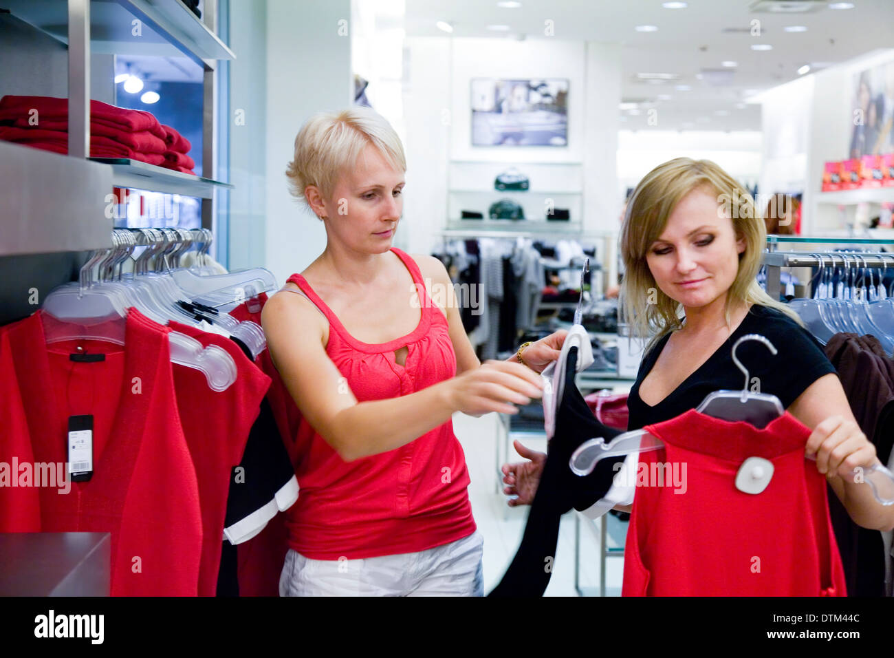 Two women looking and comparing different clothes in shop. Retail store ...