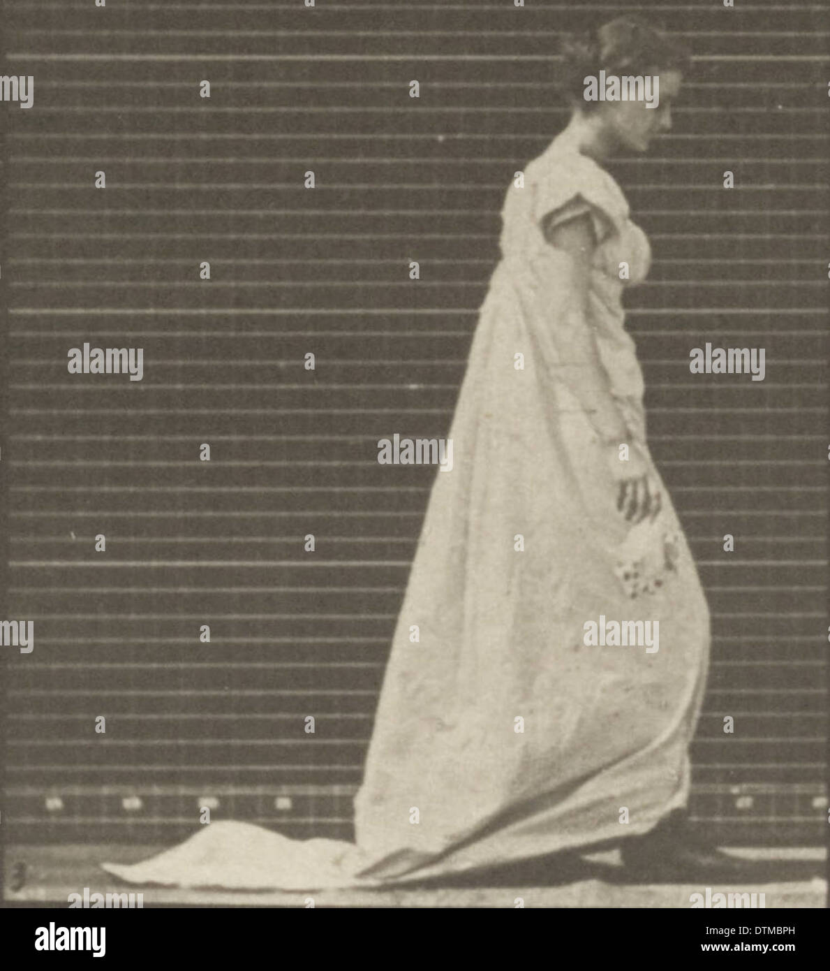 This photograph shows a woman in a long dress stooping down and lifting ...