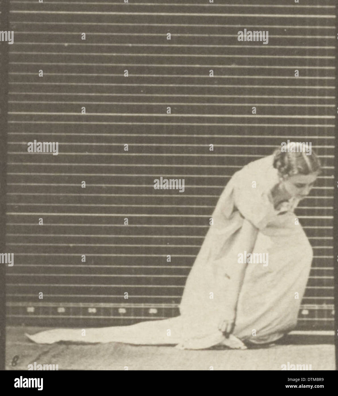 A photograph of a woman in a long dress stooping down and lifting a ...