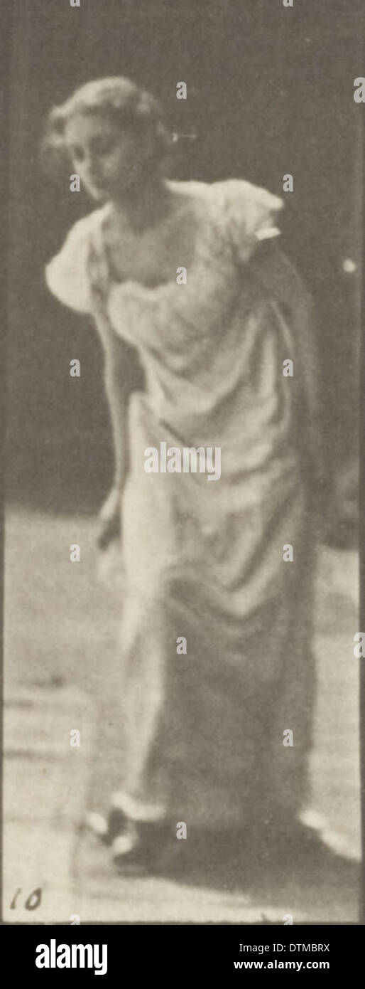 A photograph of a woman in a long dress, stooping to lift a ...