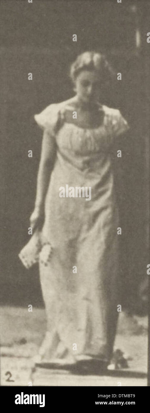 A photograph of a woman in a long dress stooping down and lifting a ...