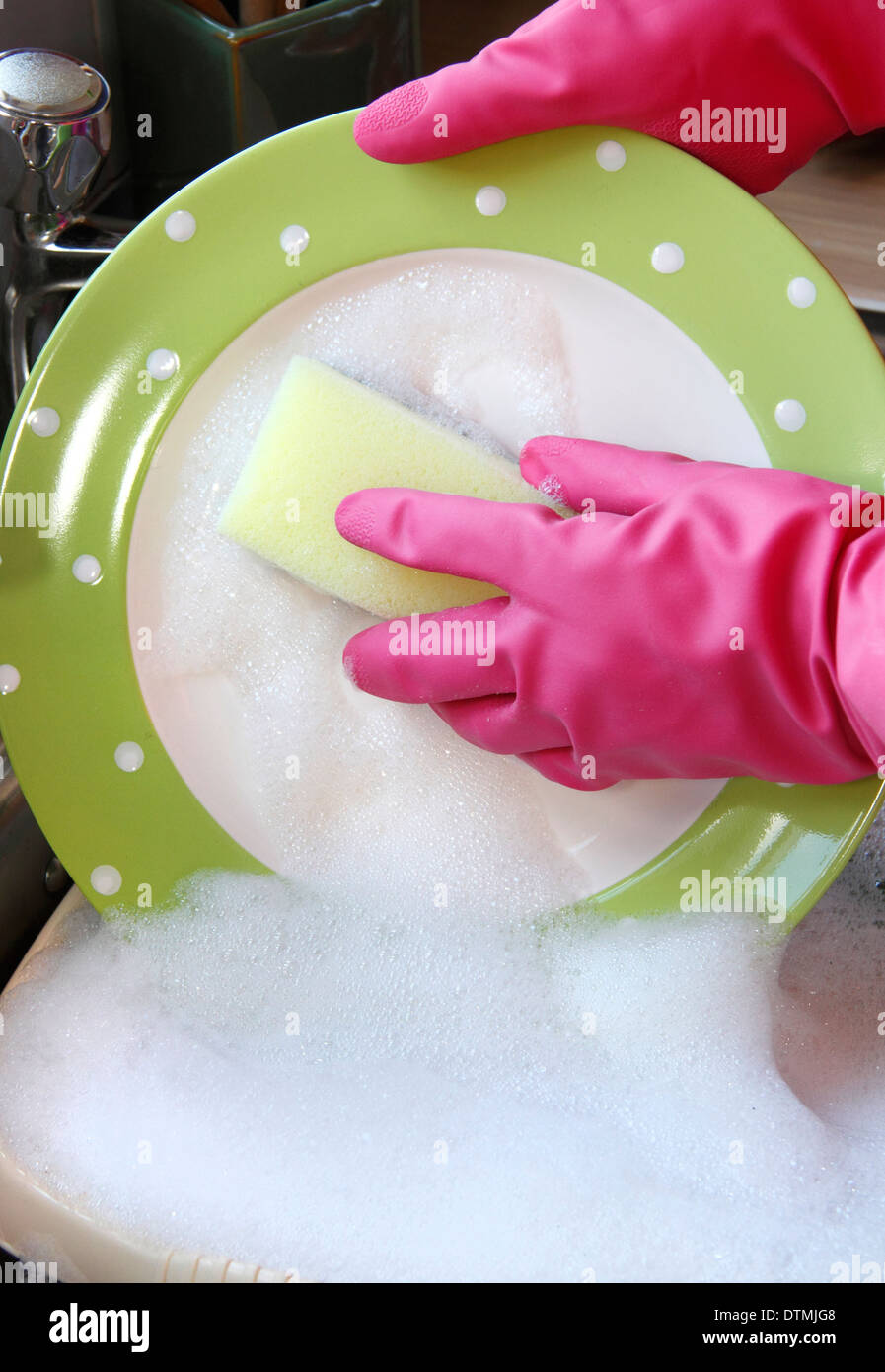 Woman wearing rubber gloves washing up the pots at the kitchen sink at ...