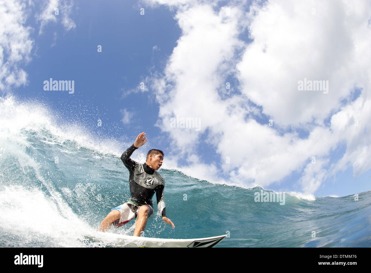 surfer surfing in the ocean with one hand up and clouds in the sky ...