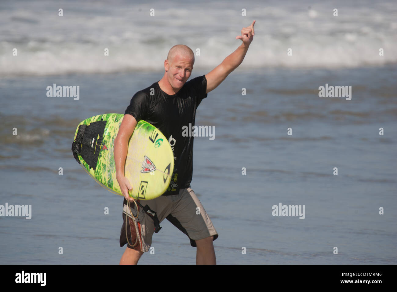 bald surfer walks along the beach with his surfboard and gives the hang ...