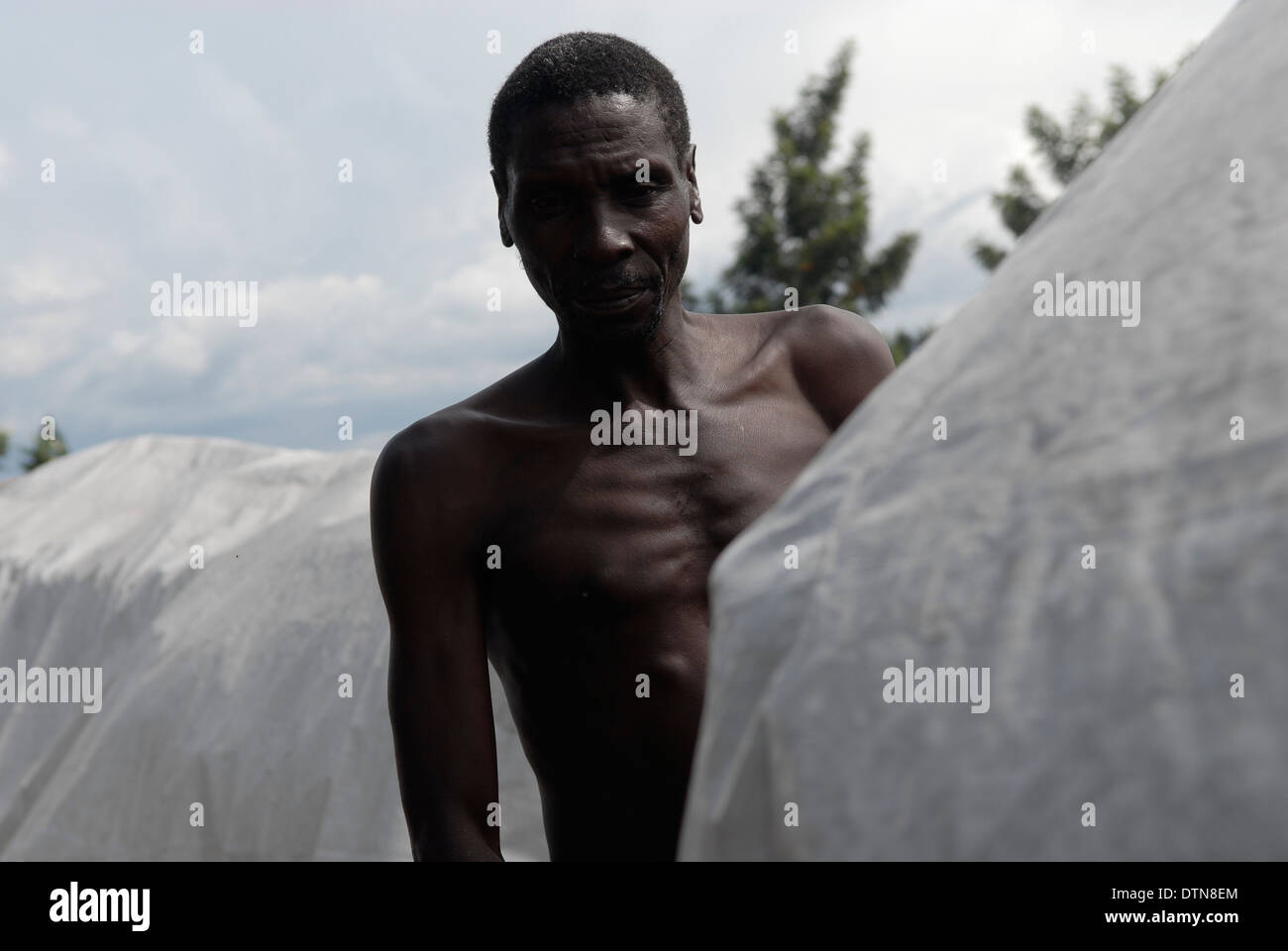 A displaced Congolese man stands amid straw huts covered with plastic ...