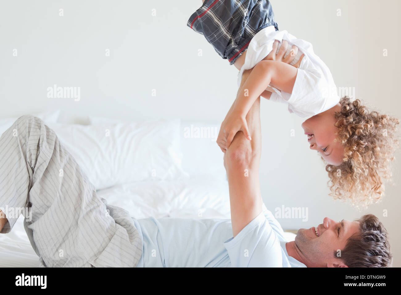 Side view of father lifting child on bed Stock Photo - Alamy