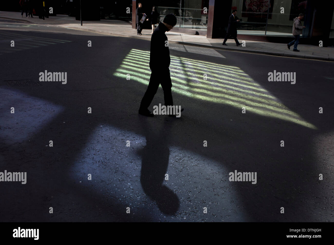 A downcast male pedestrian walks through reflected light shining from a ...