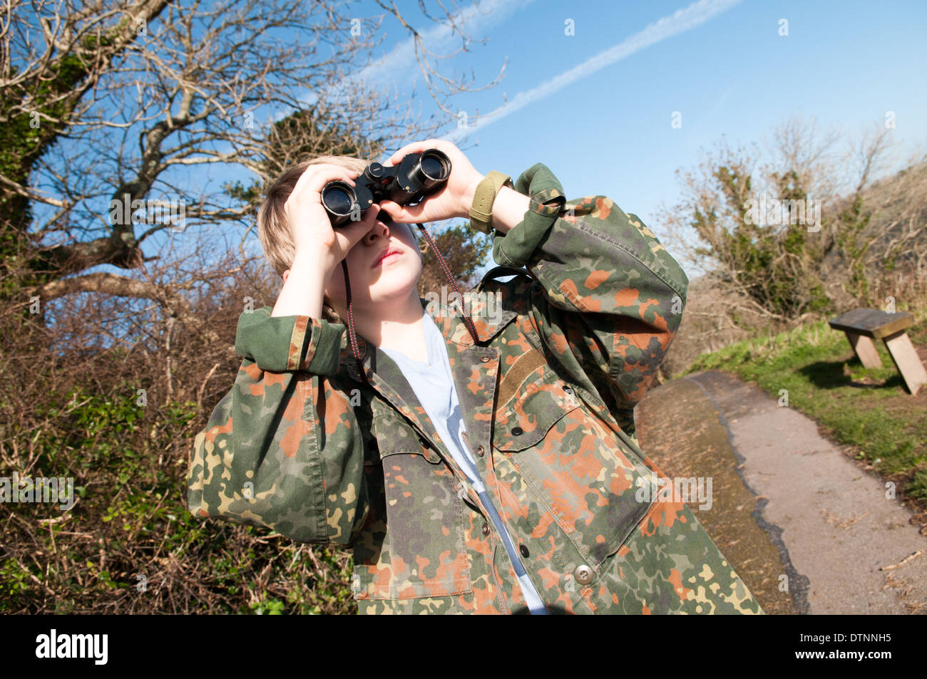 Young boy bird spotter in a camouflage jacket holds up a pair of old ...