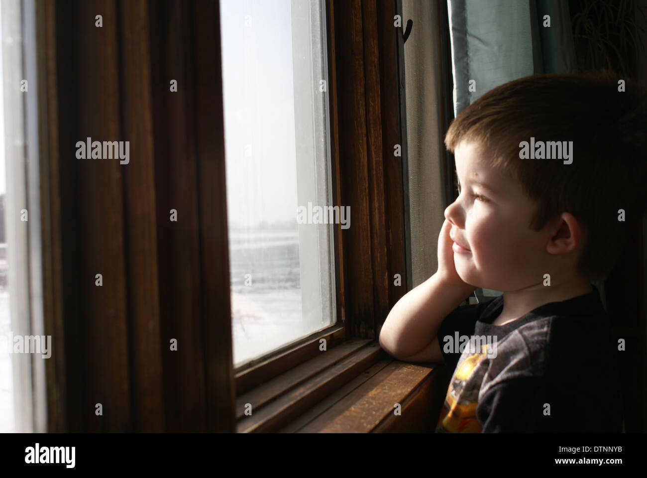 Young boy sitting inside staring out a window dreaming Stock Photo - Alamy