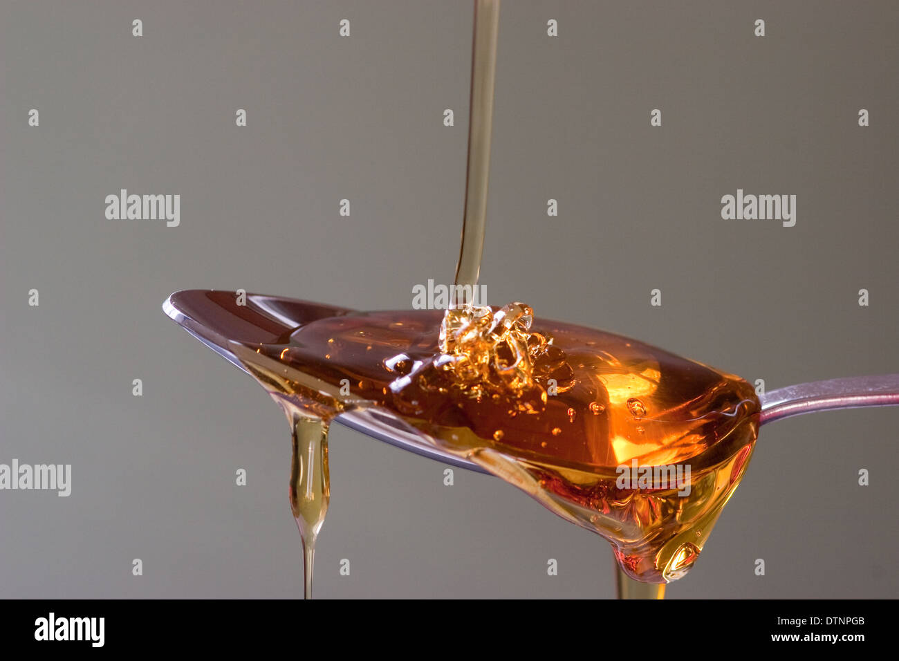 Golden syrup being poured onto silver spoon from above with a neutral ...