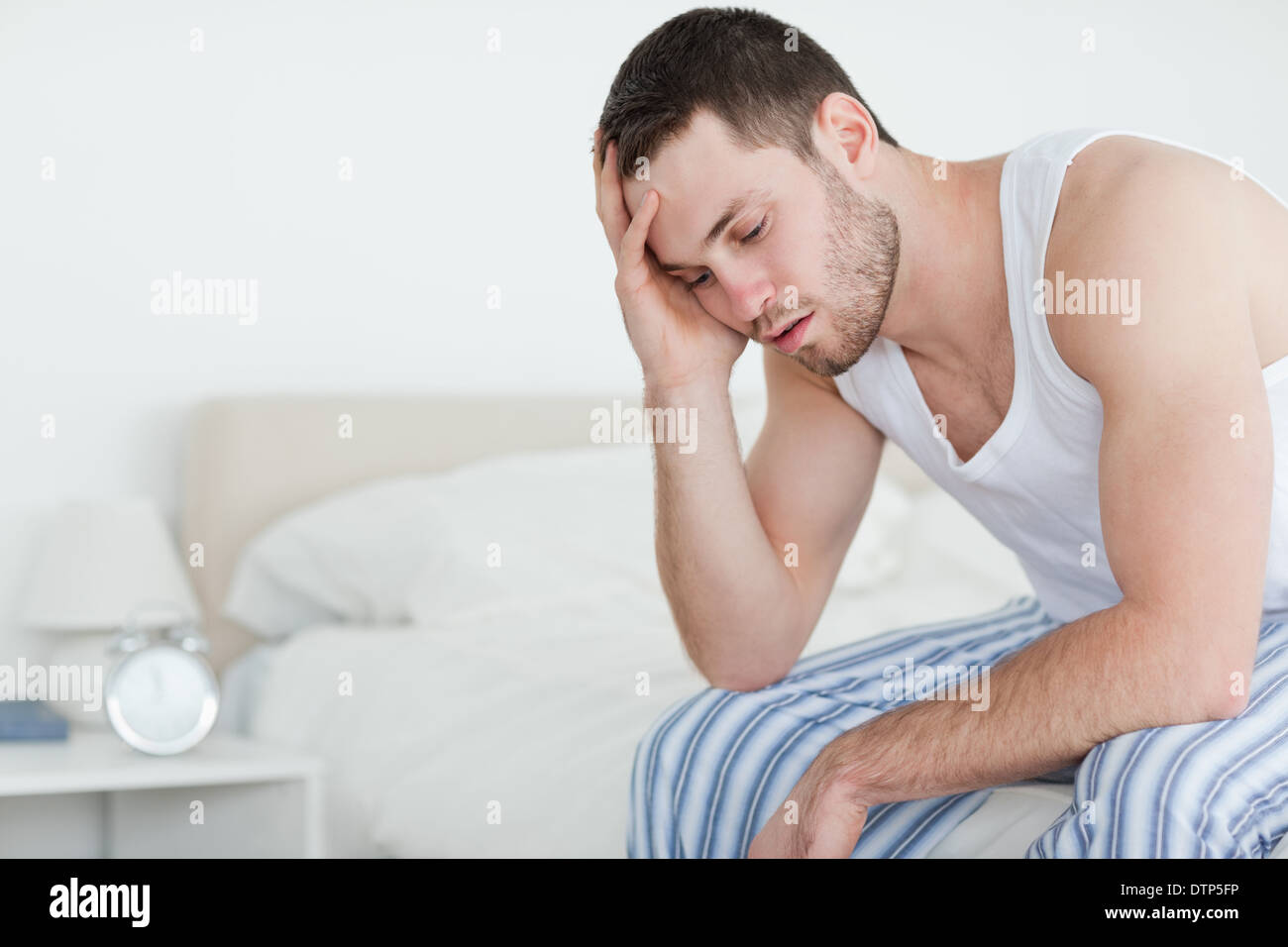 Tired young man sitting on his bed Stock Photo - Alamy