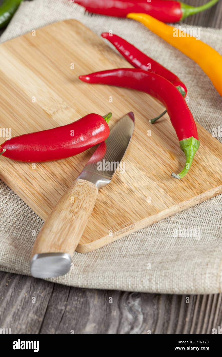 Colorful Chili Peppers with a kitchen knife on a cutting board with ...