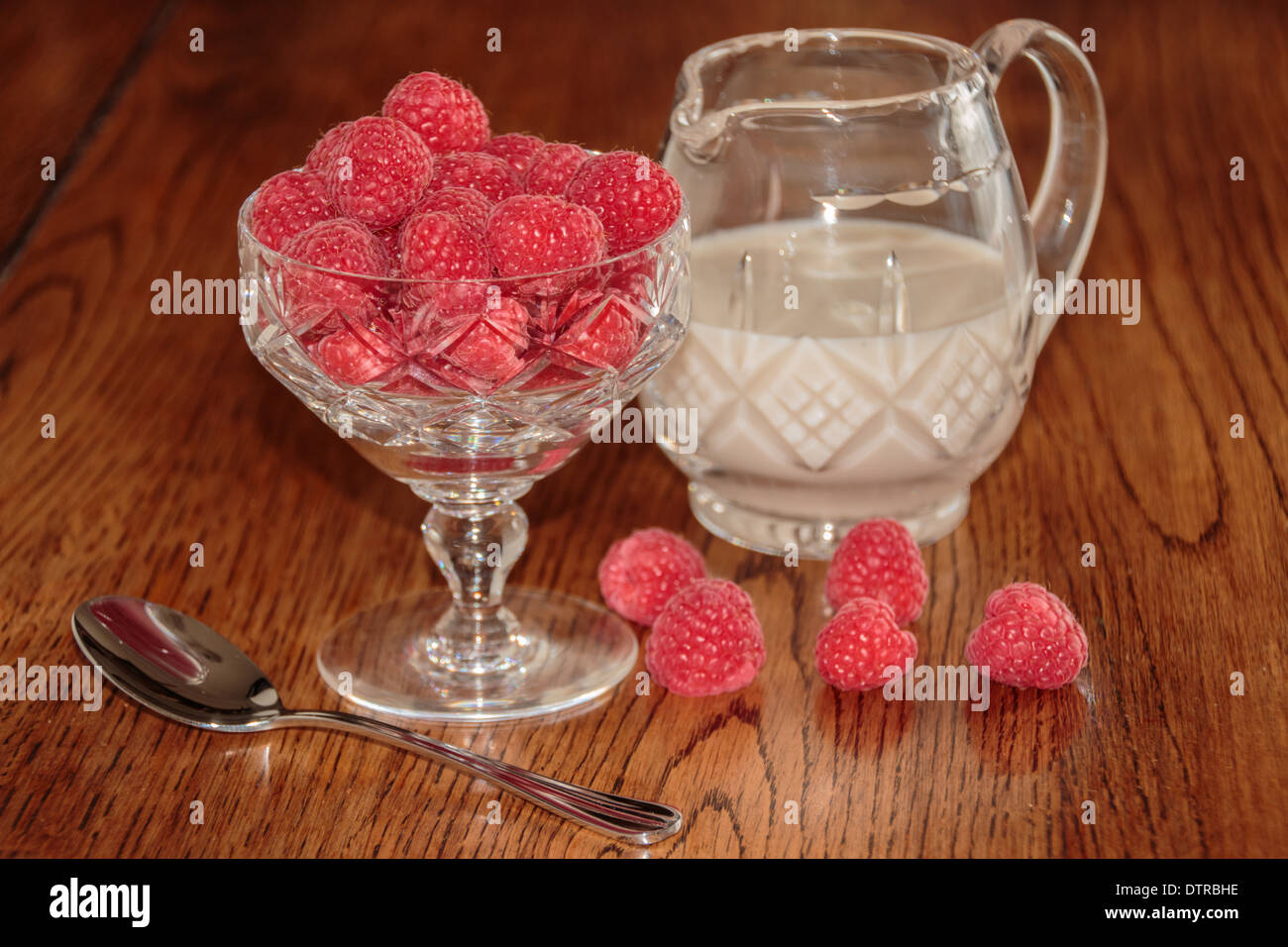 raspberries in a crystal sundae glass and cream in a jug on an oak ...