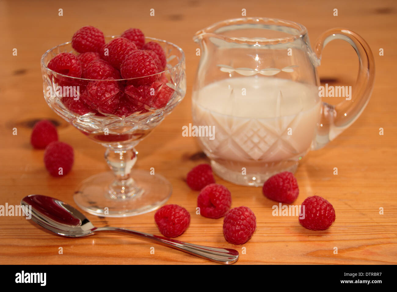raspberries in a crystal sundae glass and cream in a jug on an pine ...