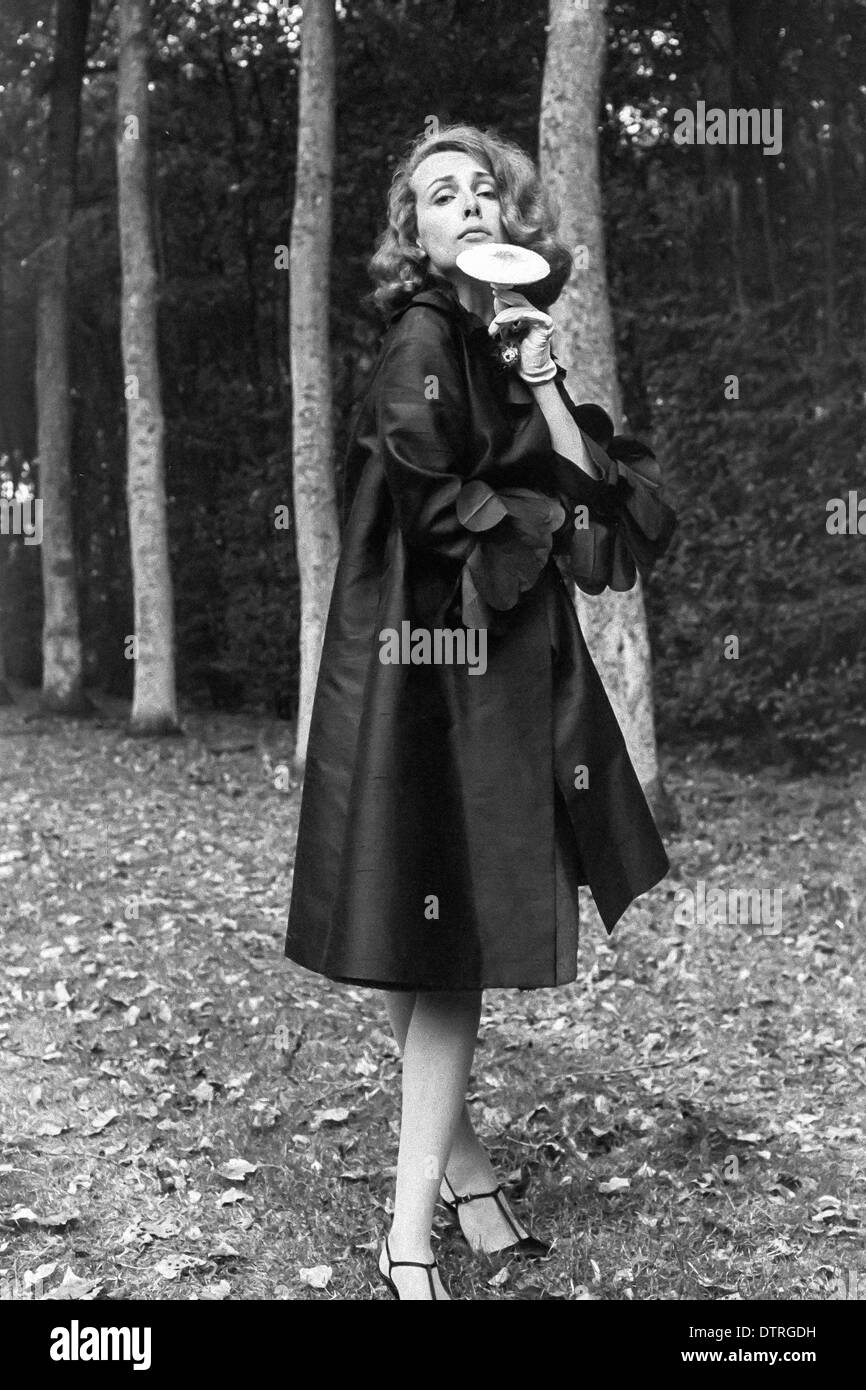 Sixties fashion model with black coat and mushroom posing in forest ...