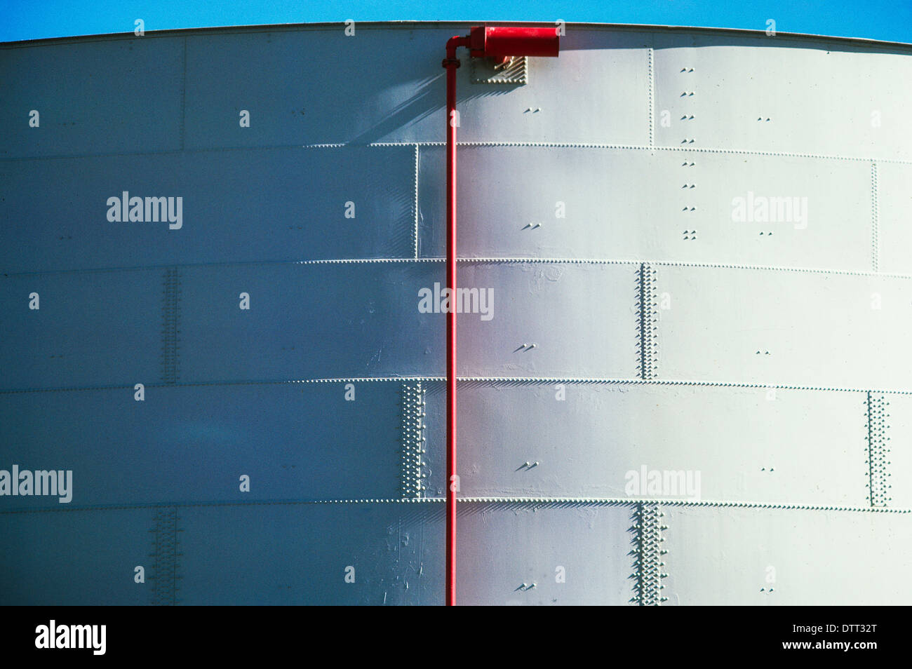 red vent pipe cuts through the facade of a white riveted water tank in ...