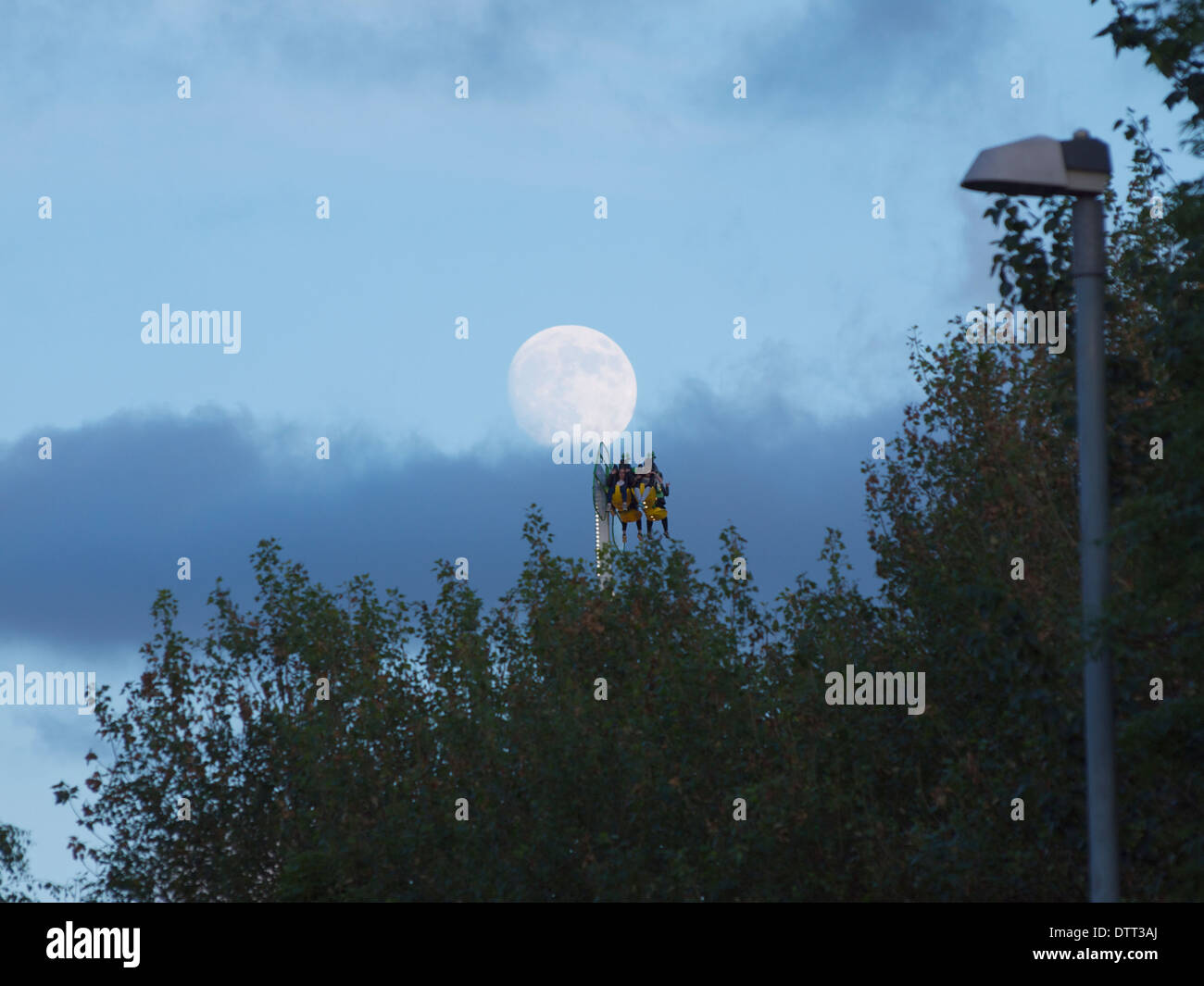 Fairground ride appearing over the top of some trees with a full moon ...