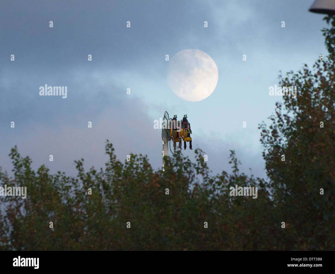 Fairground ride appearing over the top of some trees with a full moon ...