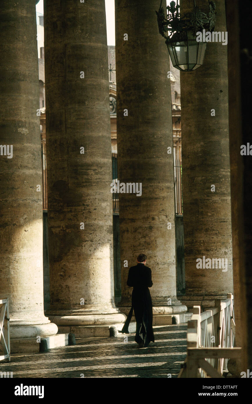 A priest in black robes walks past pillars in St Peter's Square at The ...