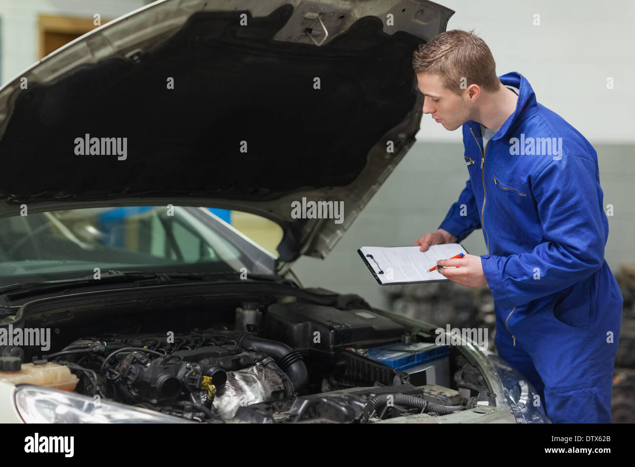 Mechanic with clipboard examining car engine Stock Photo - Alamy