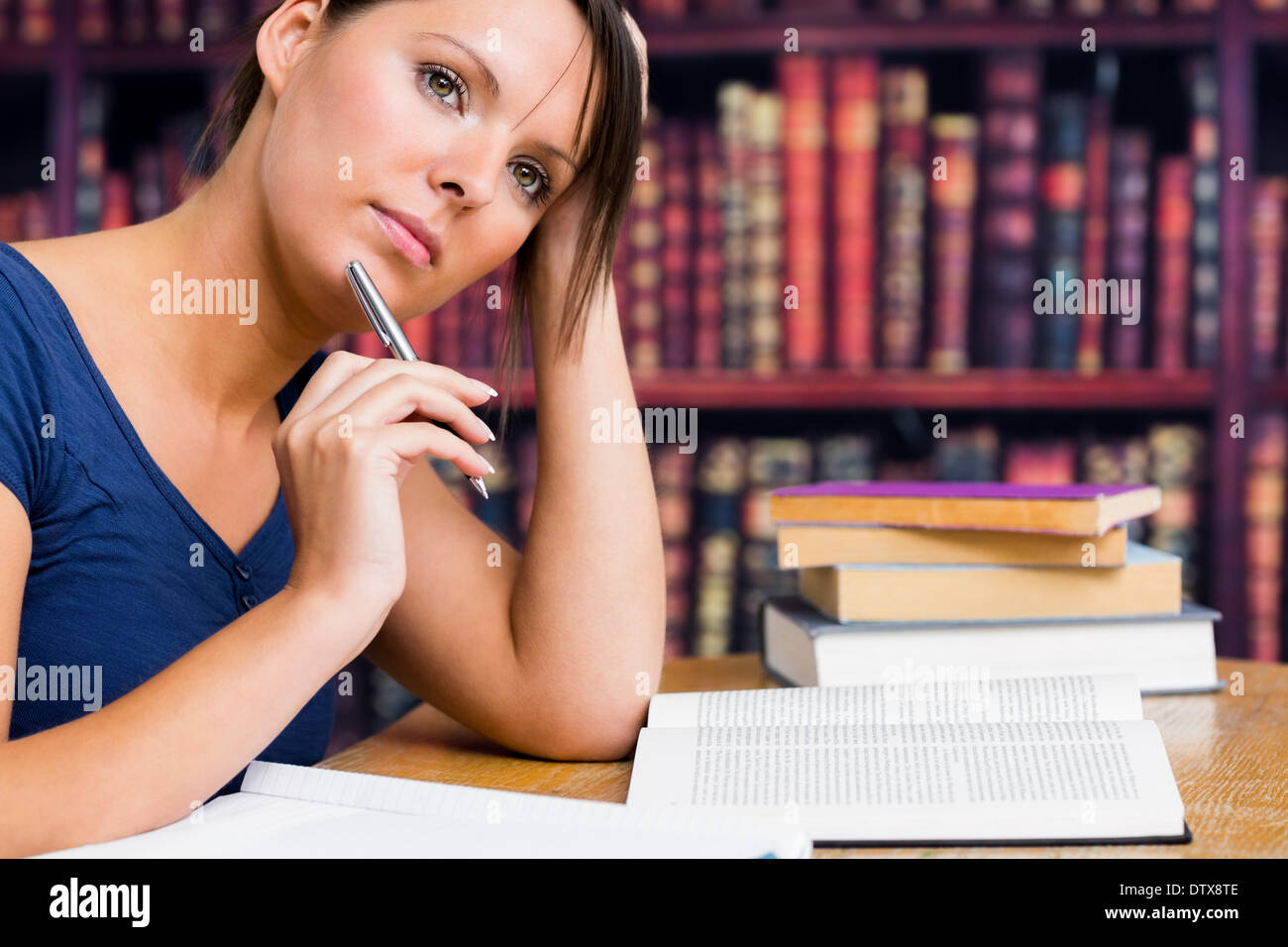Woman thinking with pen and book in library Stock Photo - Alamy