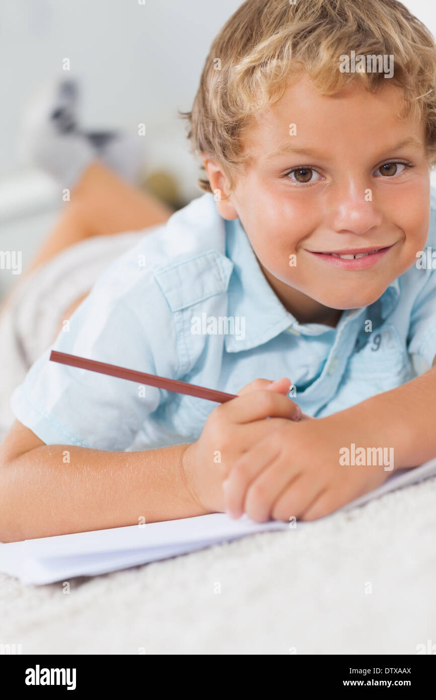 Smiling boy writing lying on the floor Stock Photo - Alamy