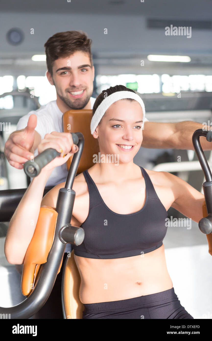 Beautiful young woman working out at the gym with the help of her ...