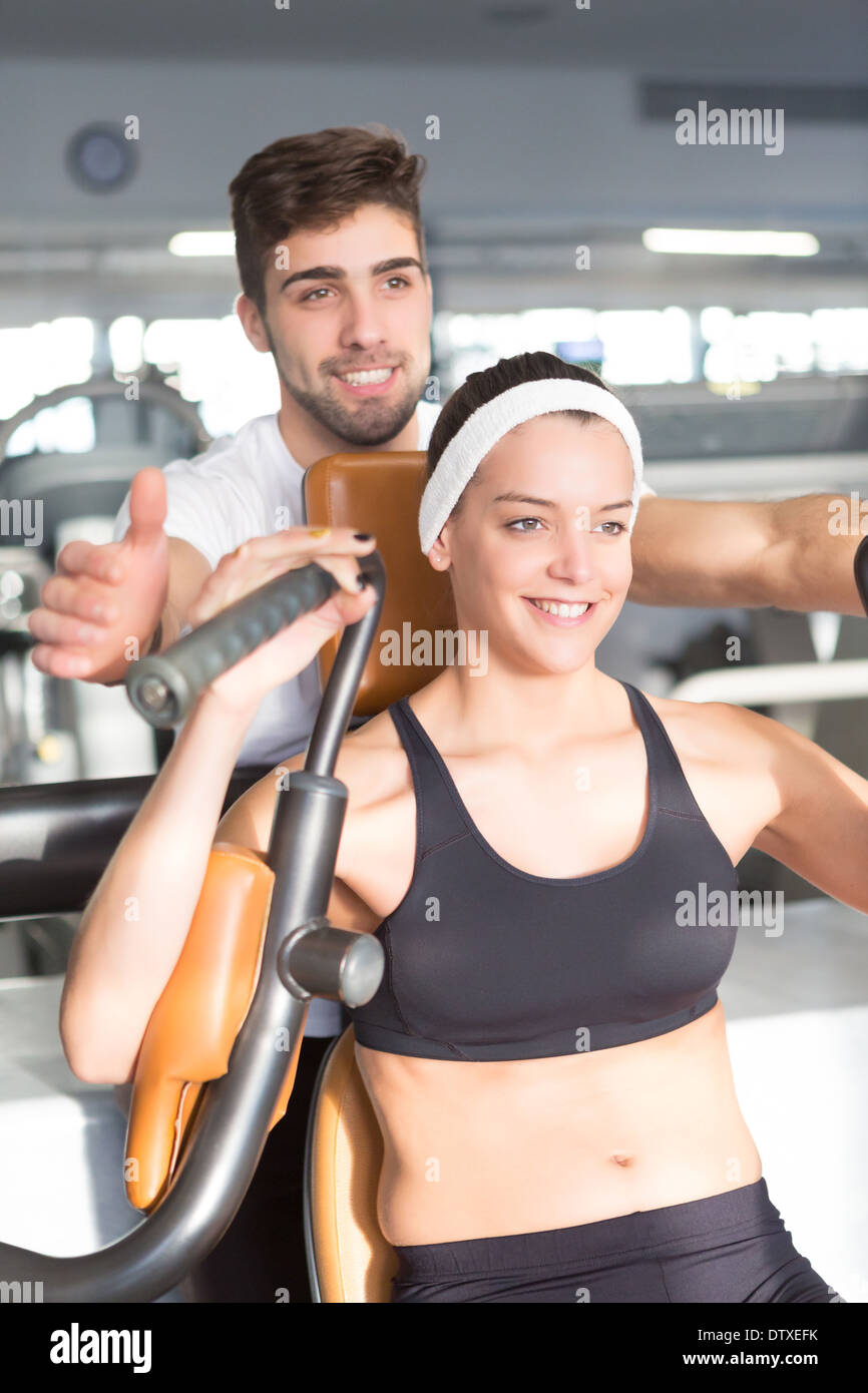 Beautiful young woman working out at the gym with the help of her ...