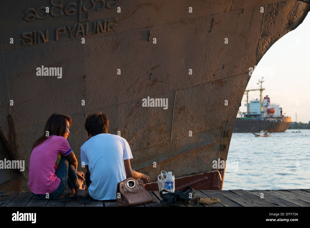 Young couple sitting at a jetty with large boat mooring. Yangon harbour ...