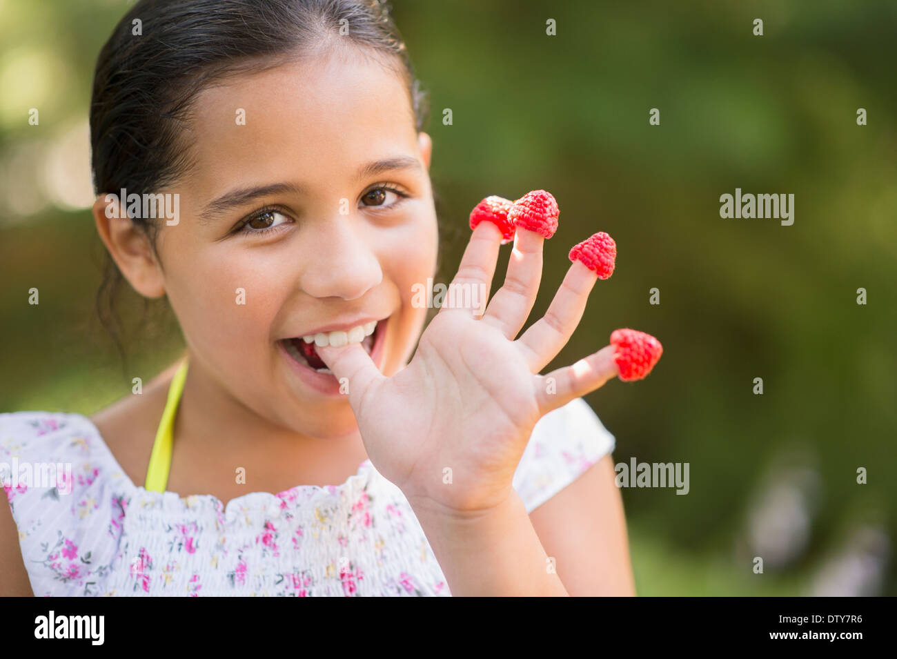 Mixed race girl eating raspberries on fingers outdoors Stock Photo - Alamy