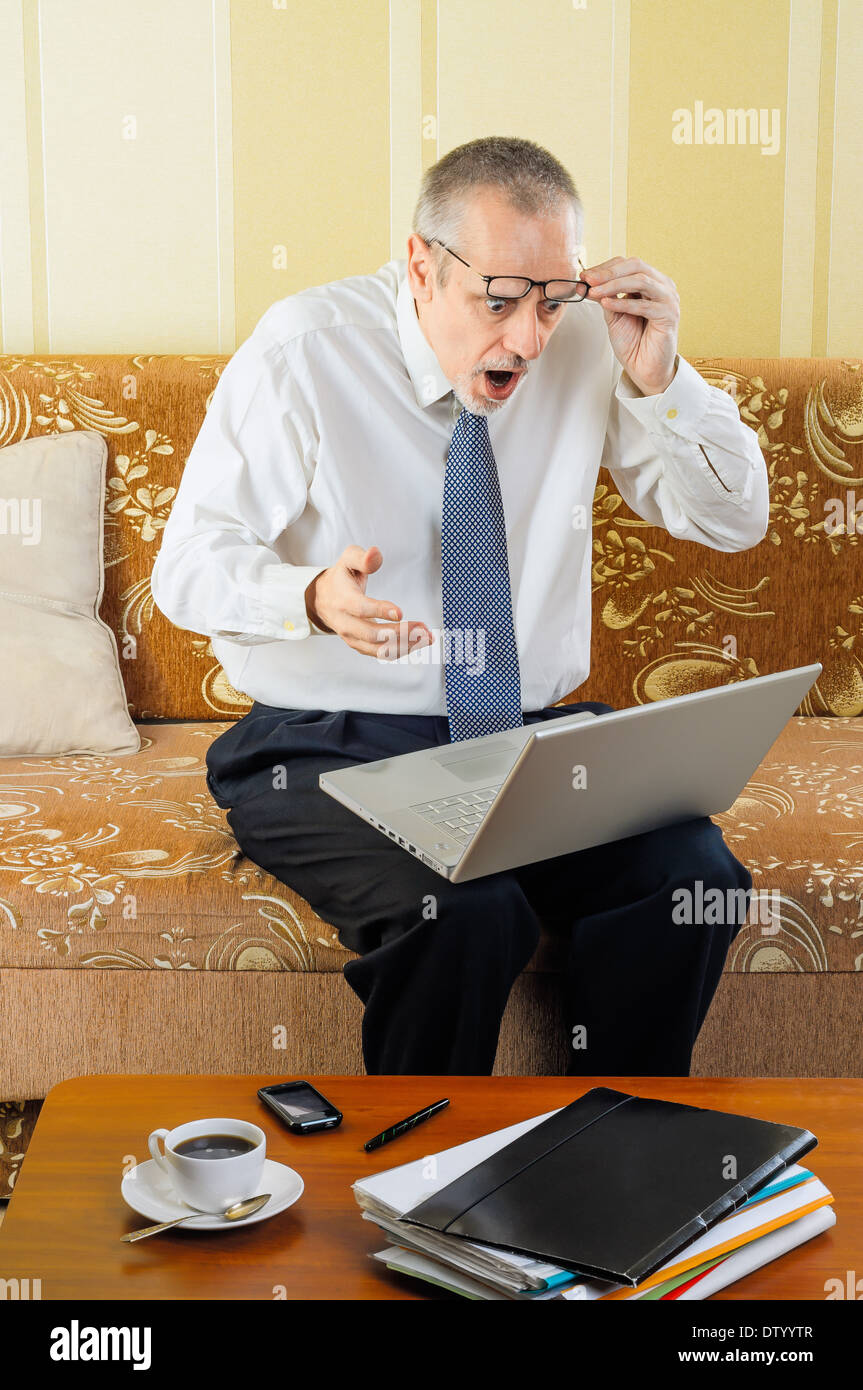 An handsome senior businessman working with computer at home, surprised ...