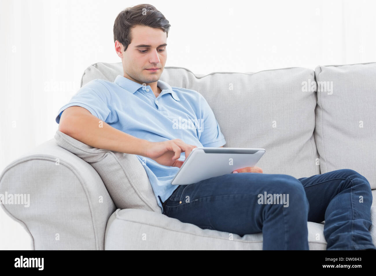 Man using his tablet sitting on a couch Stock Photo - Alamy